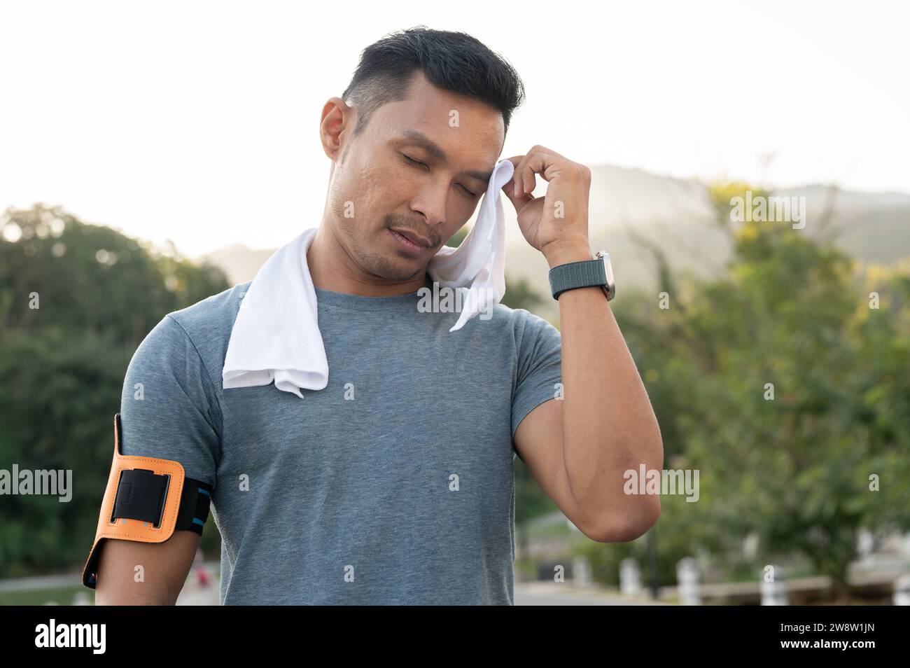 A tired Asian man in sportswear is wiping his sweat on his face while ...