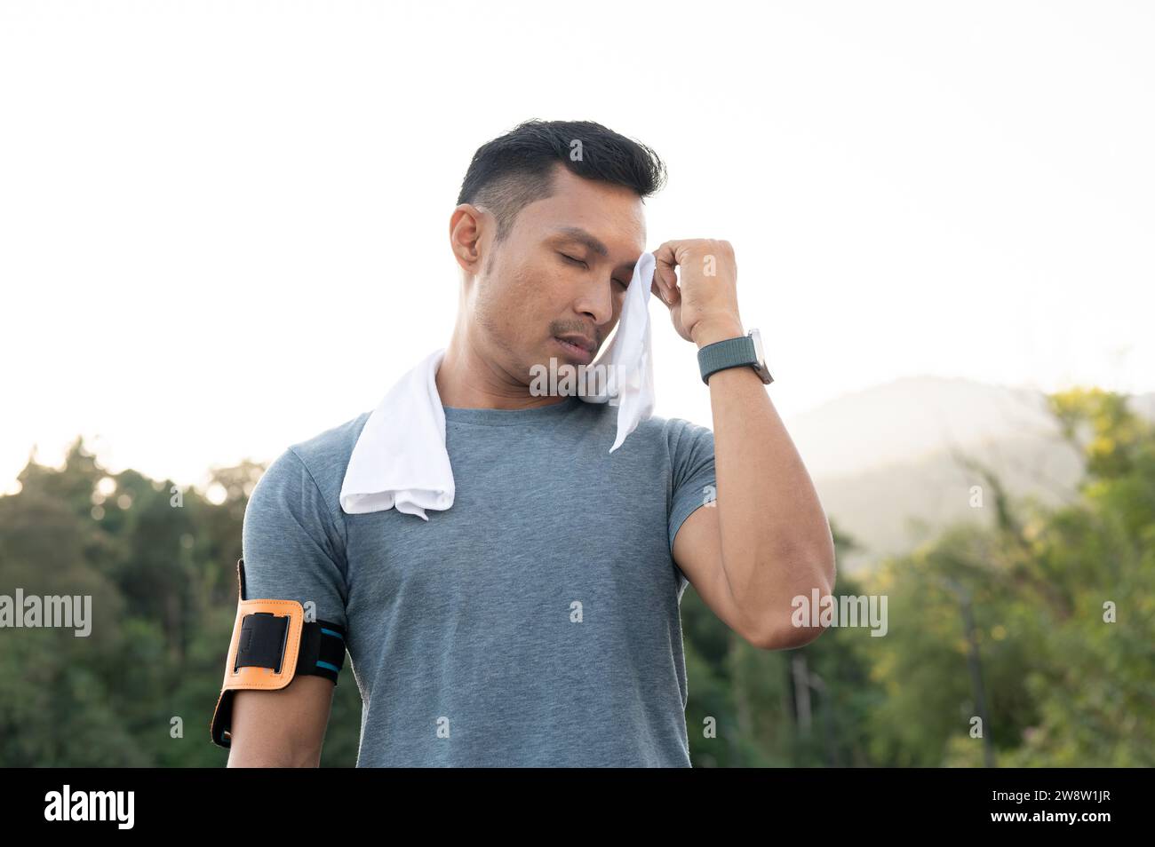 A tired Asian man in sportswear is wiping his sweat on his face while ...