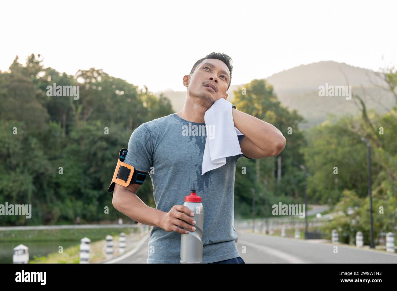 A tired Asian man is wiping his sweat on his face, resting after a long ...
