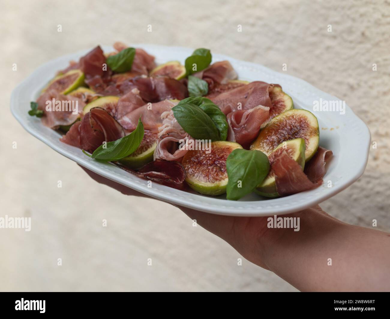 Horizontal close up of a hand holding a plate of fig and prosciutto ...