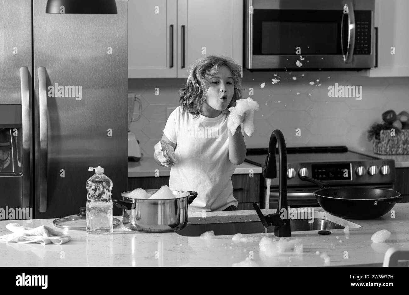 Child washing dishes near sink in kitchen. Child with sponge with dish ...