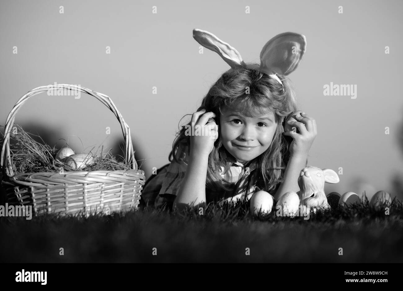 Kids boy hunting easter eggs in park laying on grass on sky background ...