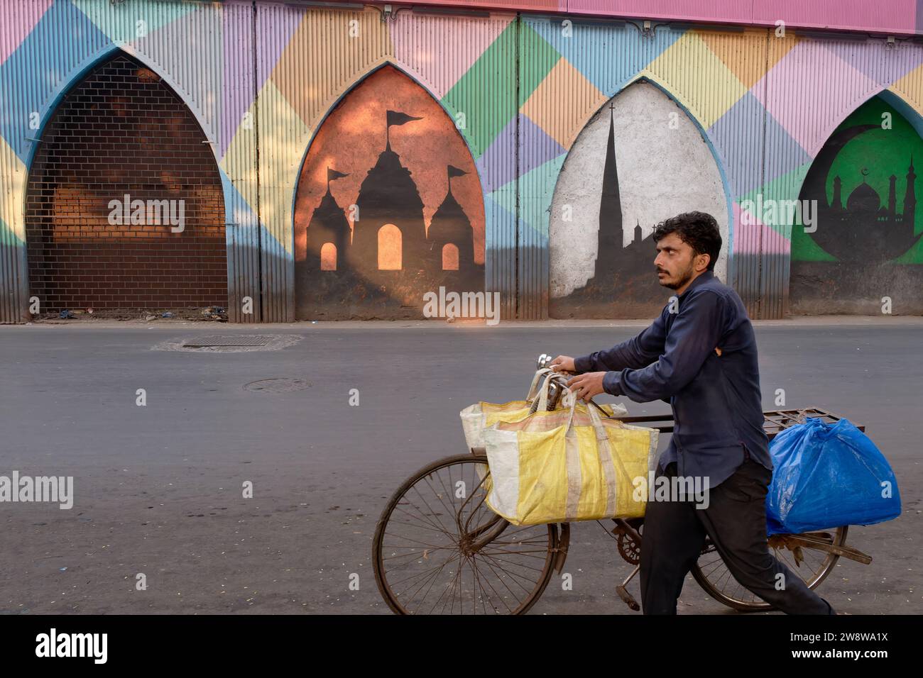 A man pushing his bicycle in Mumbai, India, laden with bags, passing ...