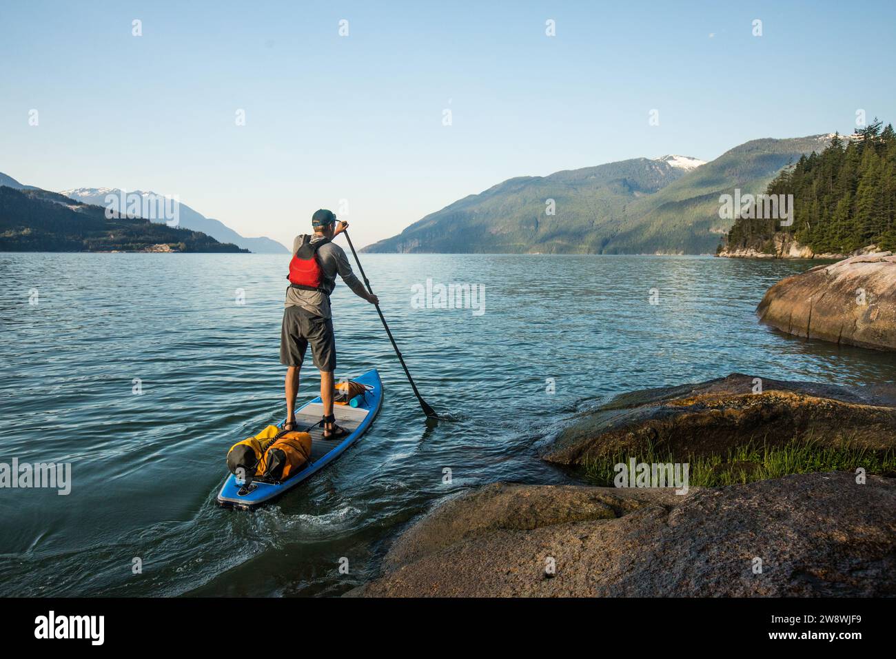 Rear view of man paddling SUP with dry bags on expedition Stock Photo ...