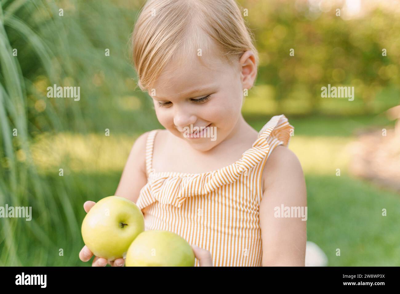 Baby girl holding green apples in her hands Stock Photo - Alamy