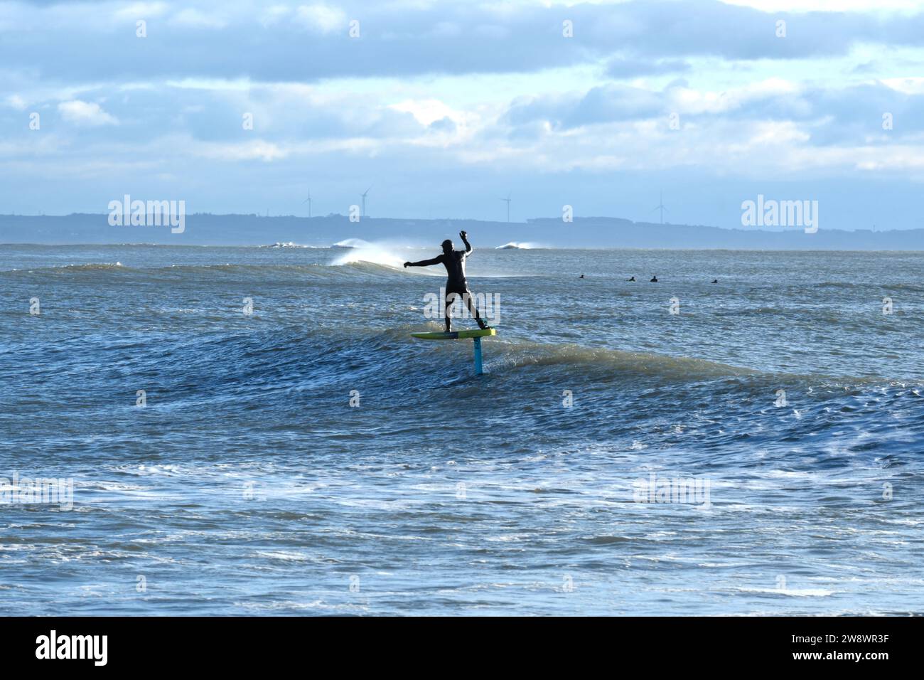 Foil surfer with hands held high flies across the surface of the wave ...