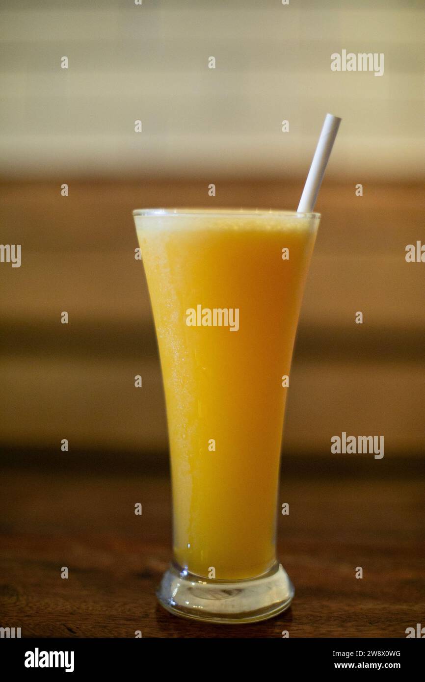 A close-up photo of a glass of orange juice with a single, bendy straw ...