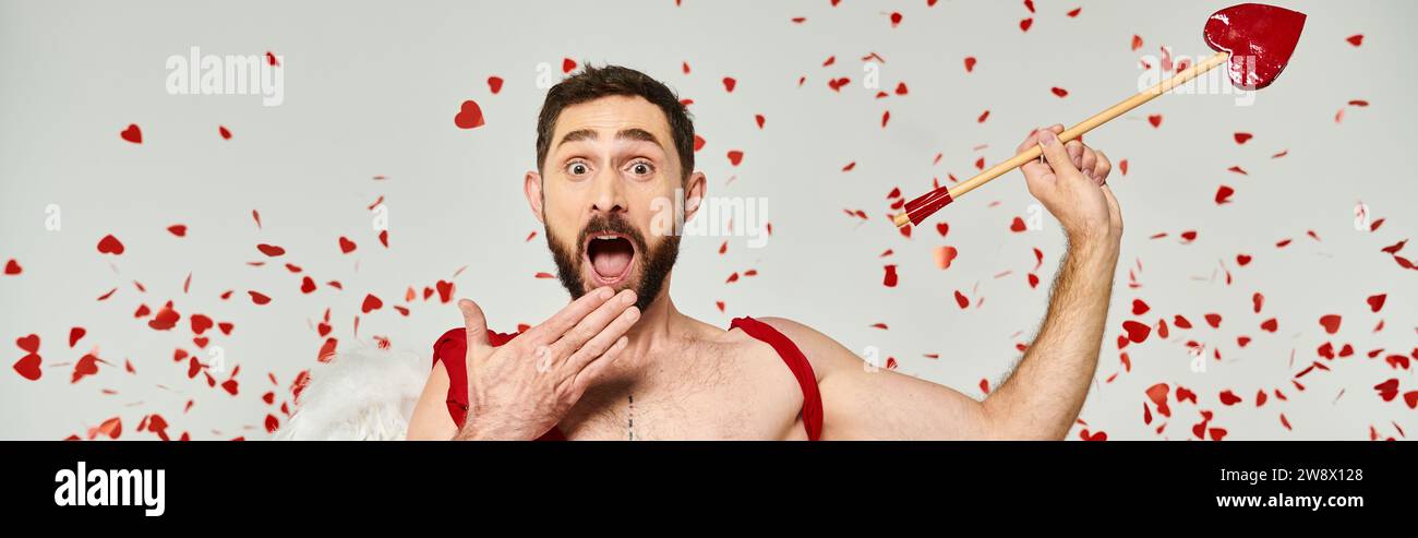 astonished cupid man holding arrow and covering open mouth with hand ...