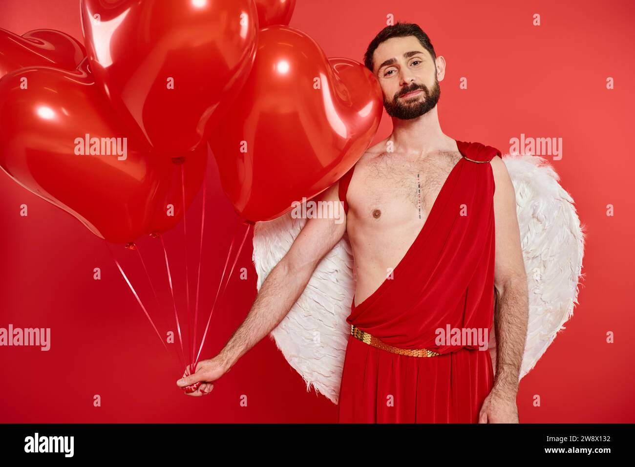 dreamy and happy cupid man with heart-shaped balloons looking at camera ...
