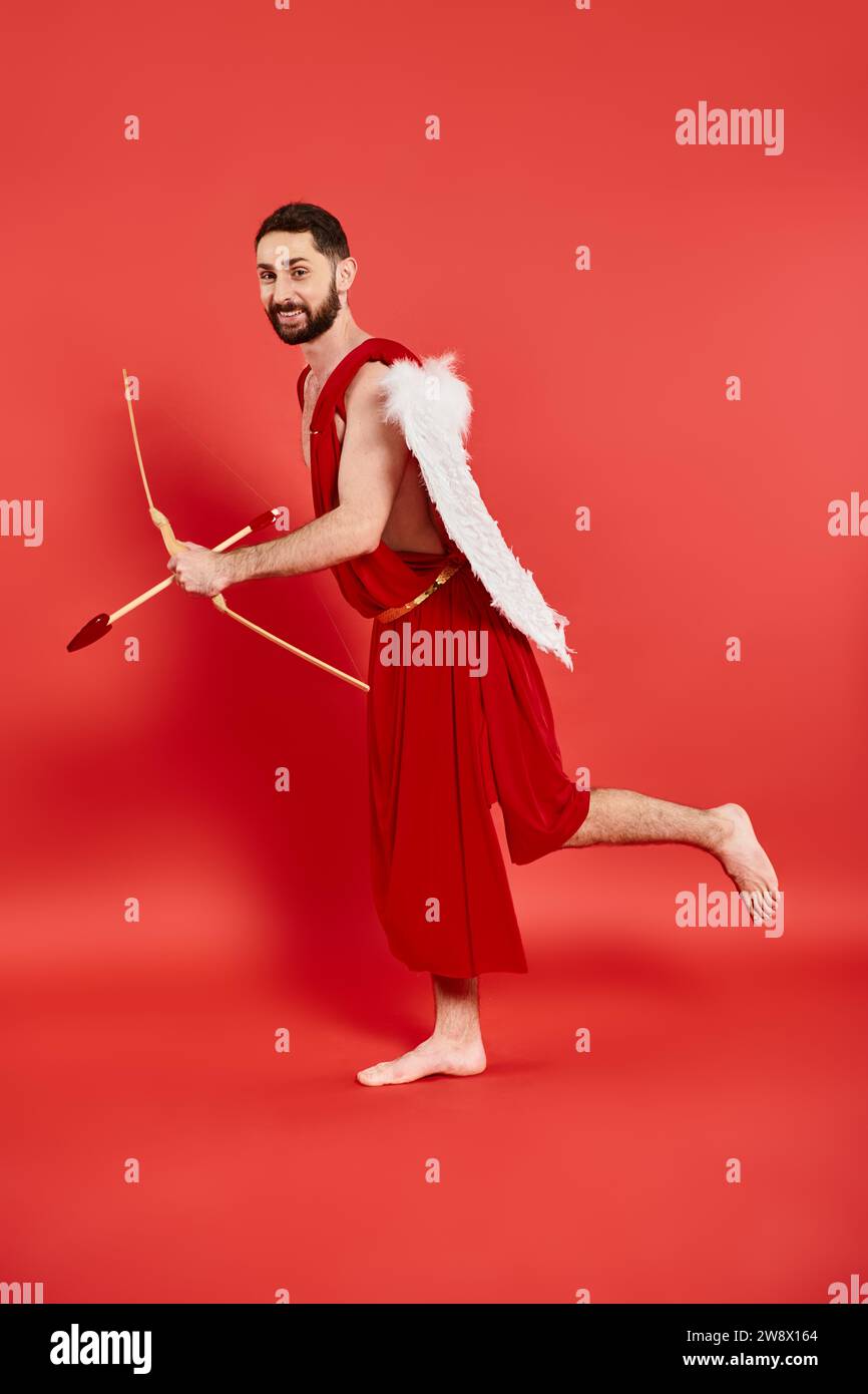 funny bearded man in cupid costume running with bow and arrow on red ...
