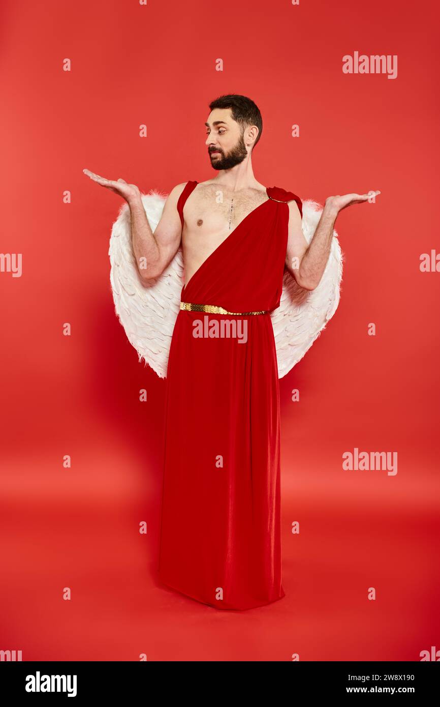 full length of man dressed as cupid looking at his open palms on red ...