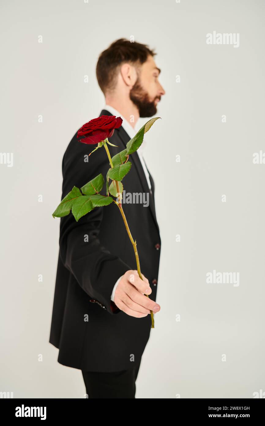 side view of bearded man in black suit with red rose in outstretched ...