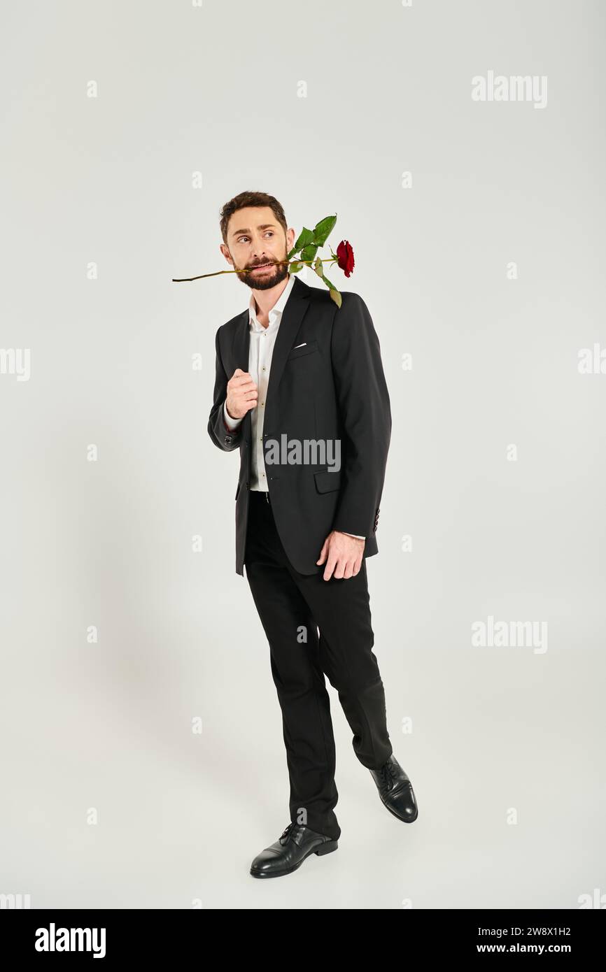 full length of bearded man in black suit standing with red rose in ...
