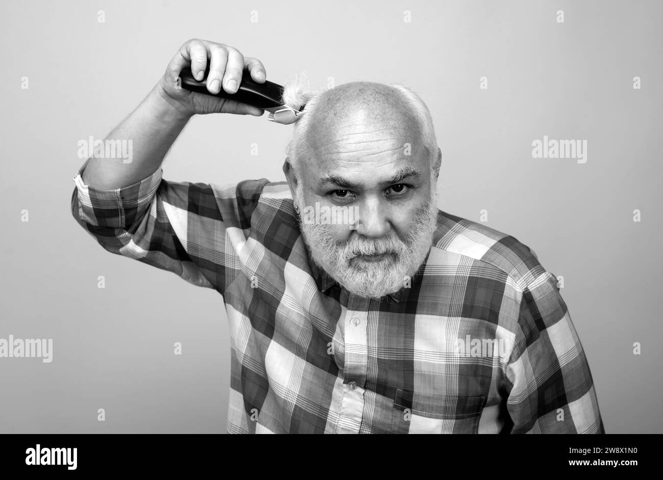 Bearded man cutting his own hair with a clipper. Middle aged bald man ...