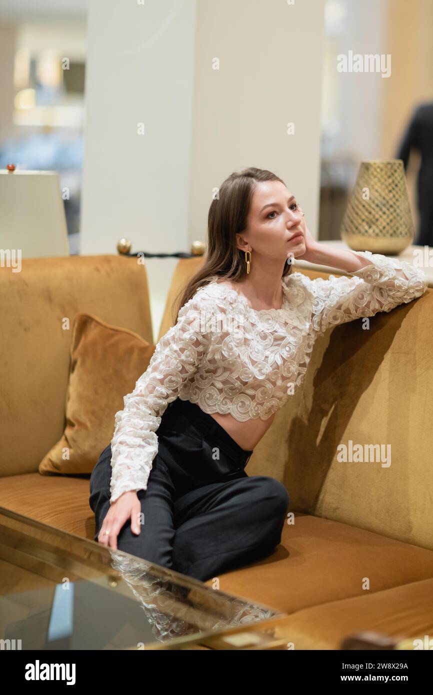 relaxed fair haired woman in lace top and pants sitting on couch in ...