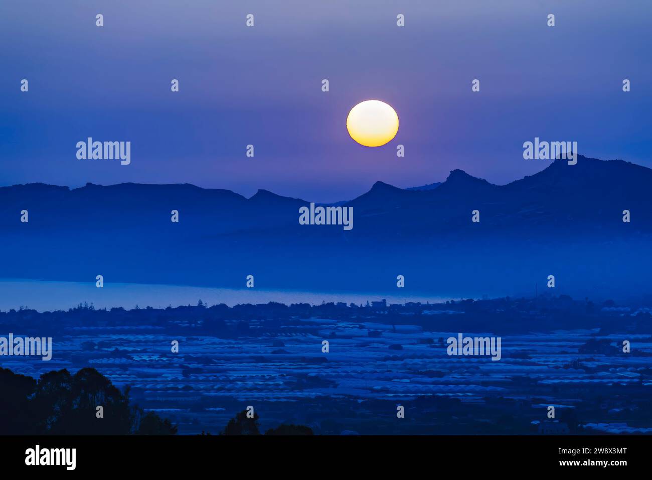 Full moon rising above serene blue mountains and silhouetted peaks ...