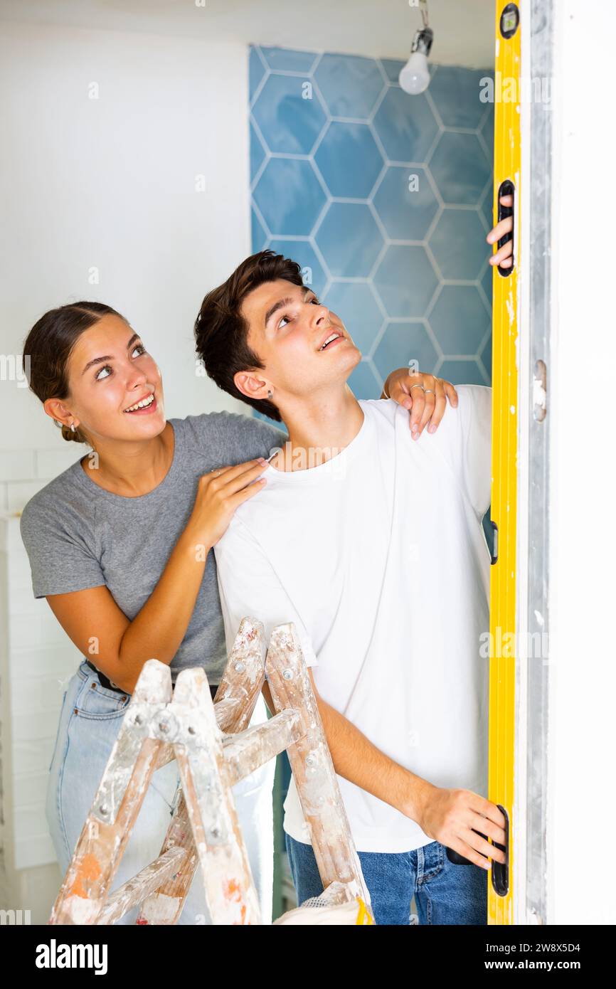 Positive couple checking laid tiles on wall with level meter in room ...