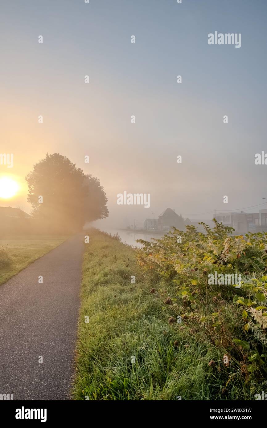 The image showcases a serene sunrise scene along a canal path. The sun ...