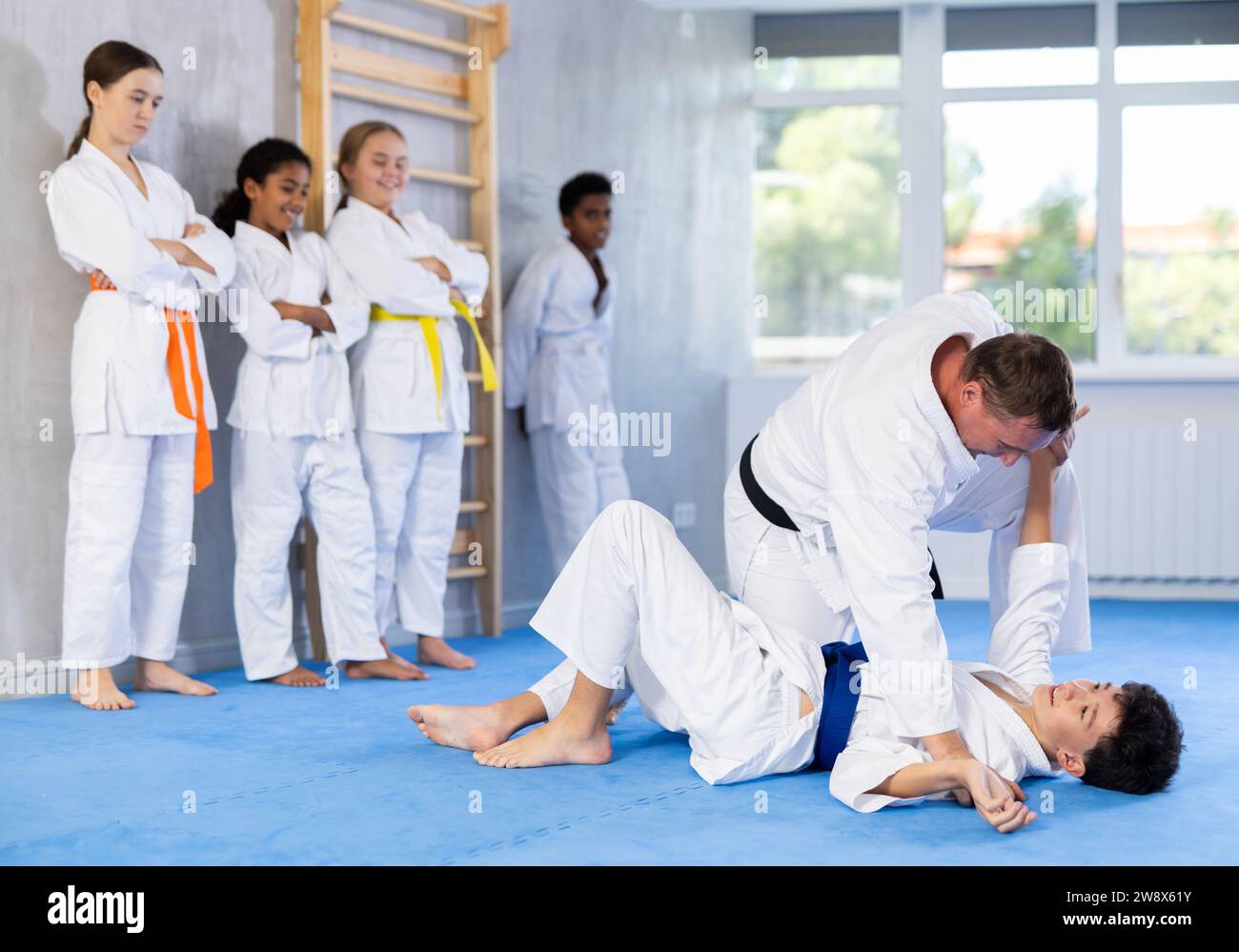 Judo coach shows fighting techniques in sparring with a boy for group ...