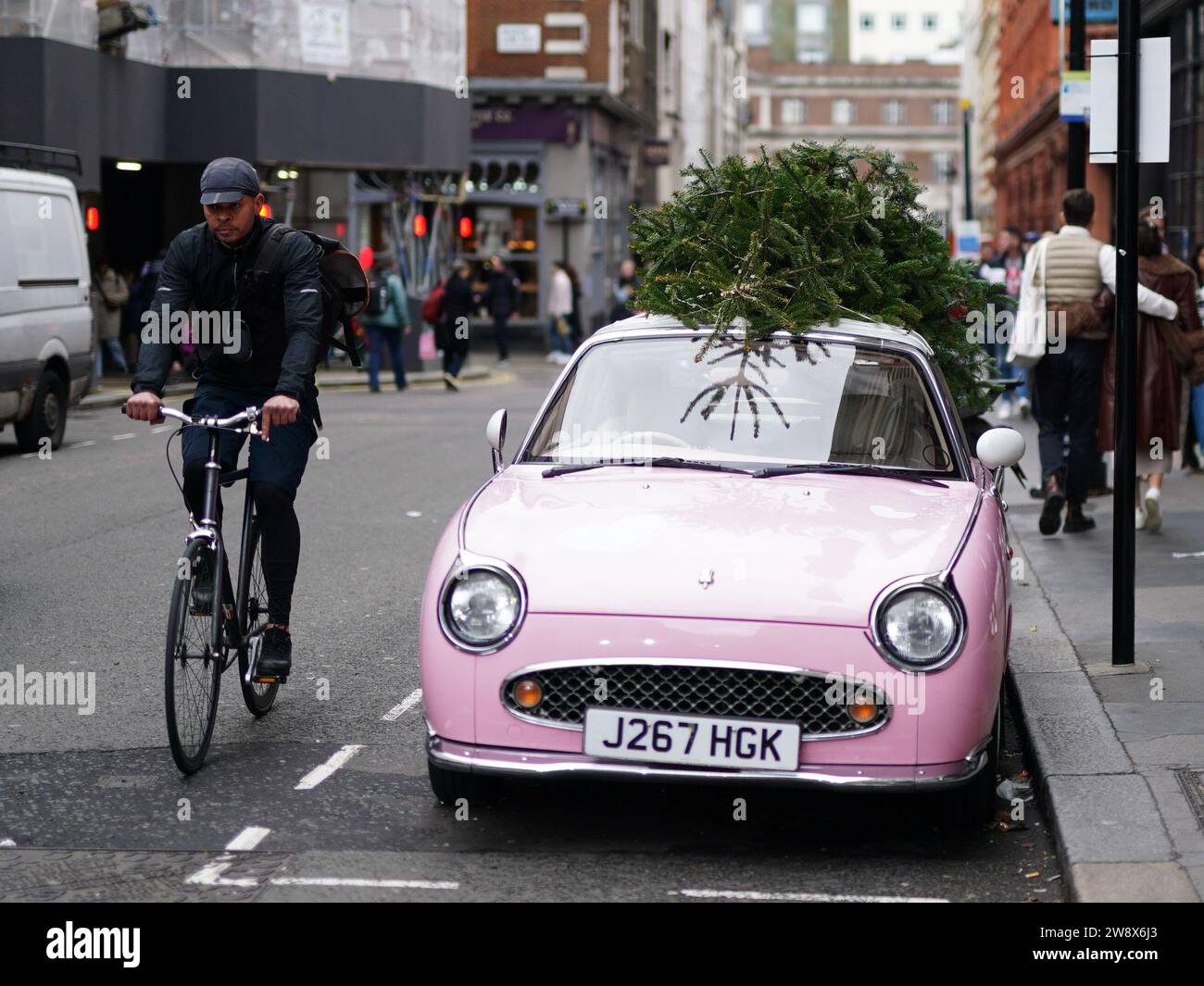 People look at a pink Nissan Figaro with a Christmas tree on top of the ...