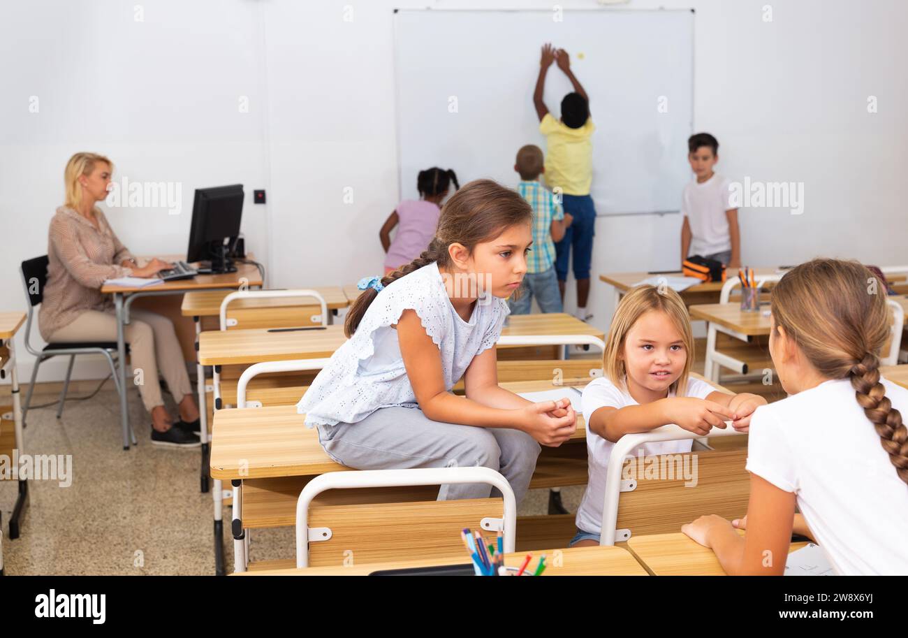 Happy preteen schoolchildren communicating during recess in classroom ...