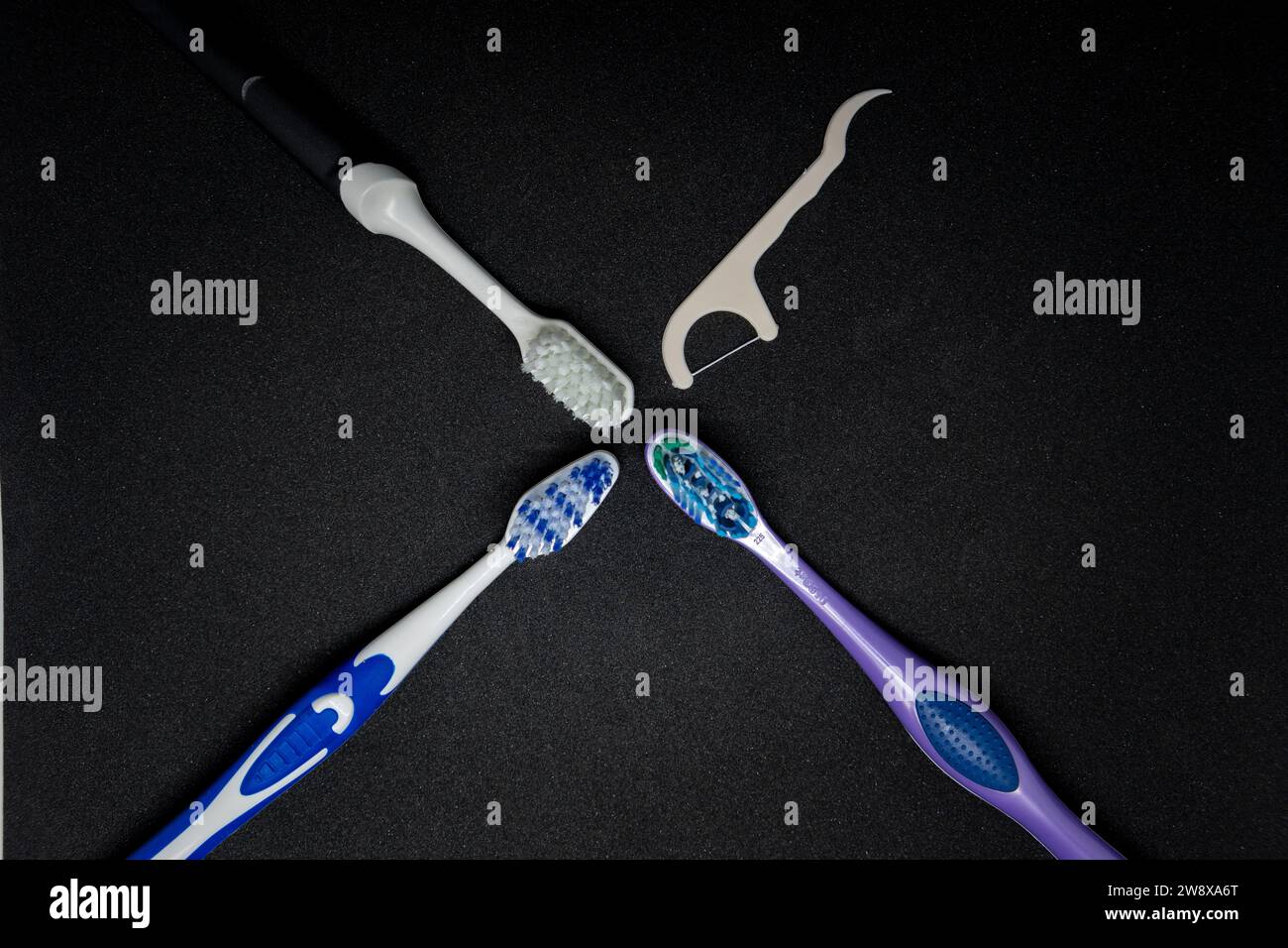 Three toothbrushes and a floss instrument aligned in an x Stock Photo ...