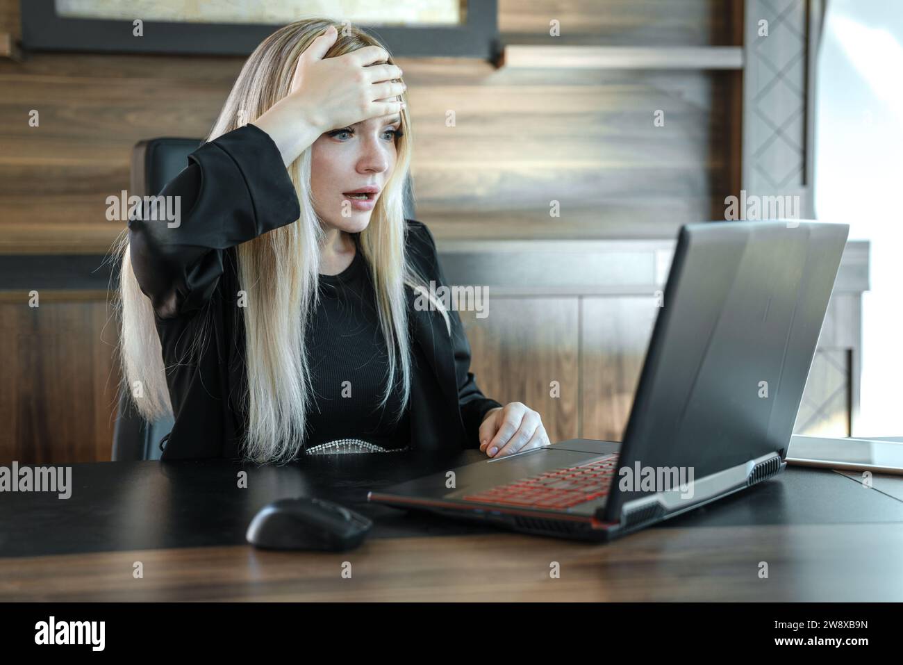 Businesswoman with frightened expression looks at laptop screen ...