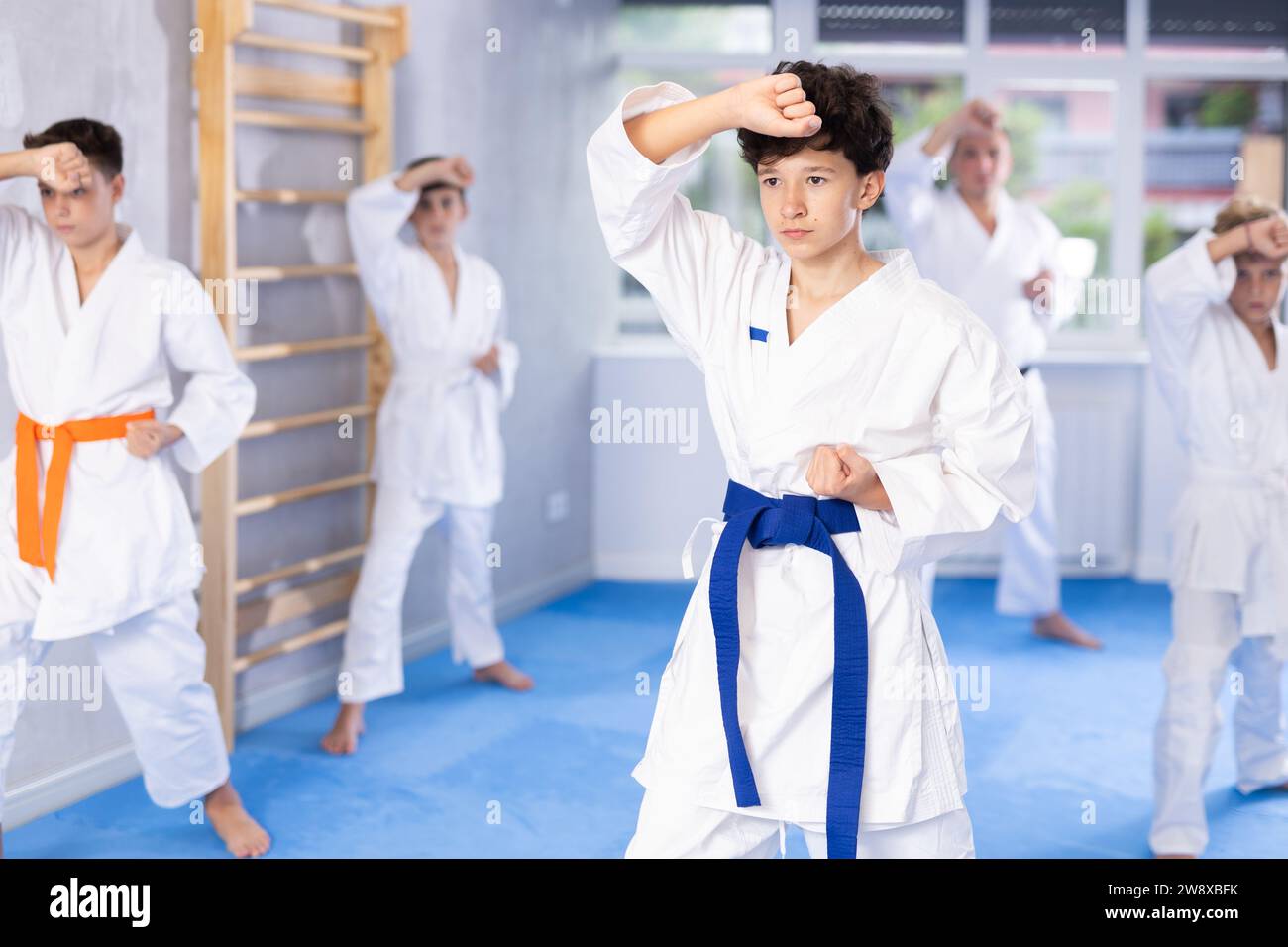 Preteen attendee of karate classes practicing kata standing in row with ...