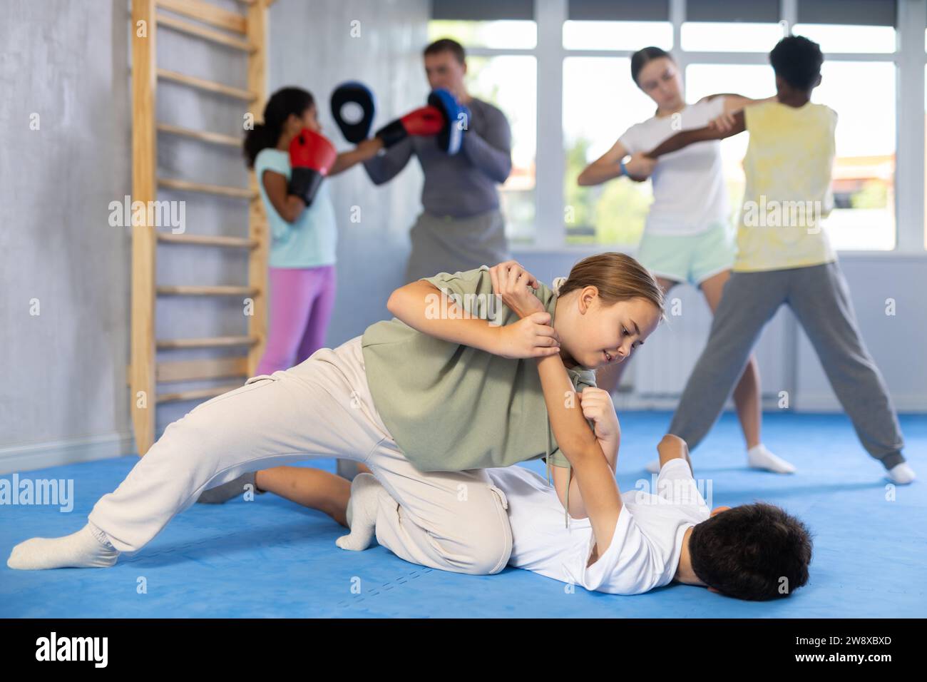 Tween girl applying armlock to face-down boy in mock fight at self ...