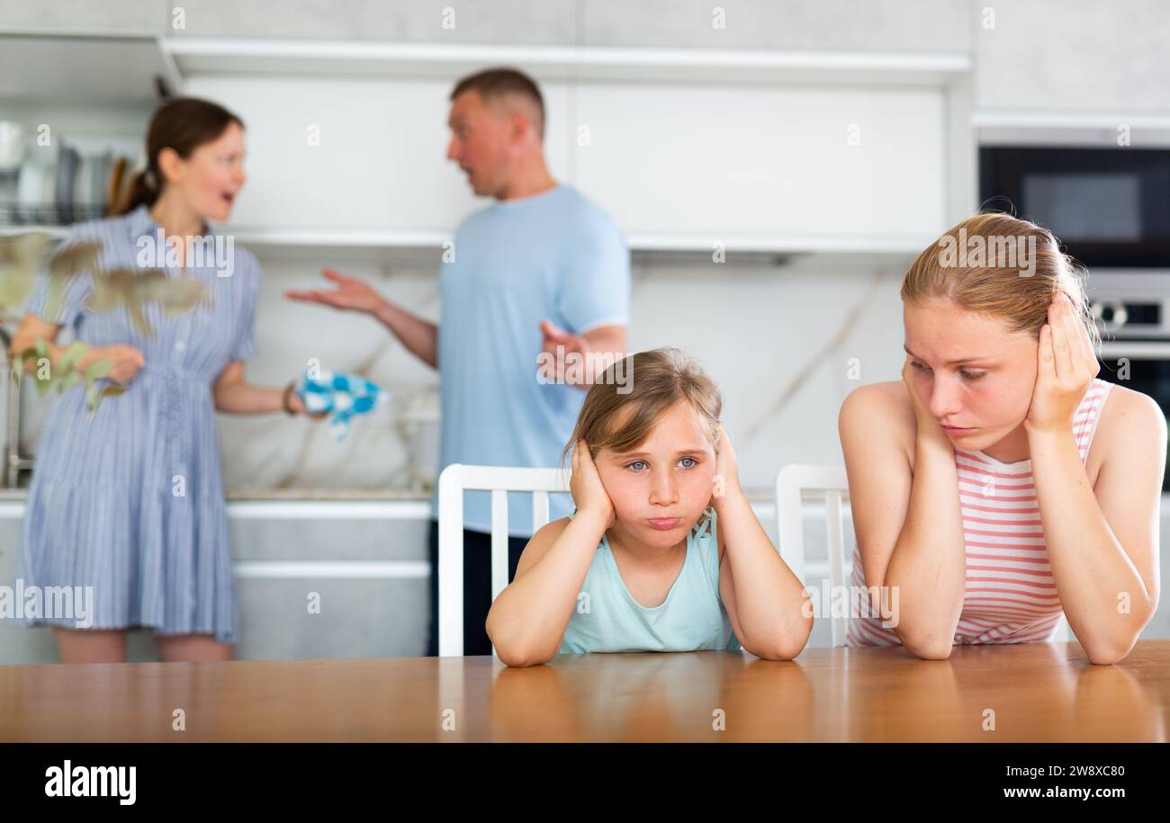 Upset teenage girls sitting in kitchen while parents quarreling Stock ...