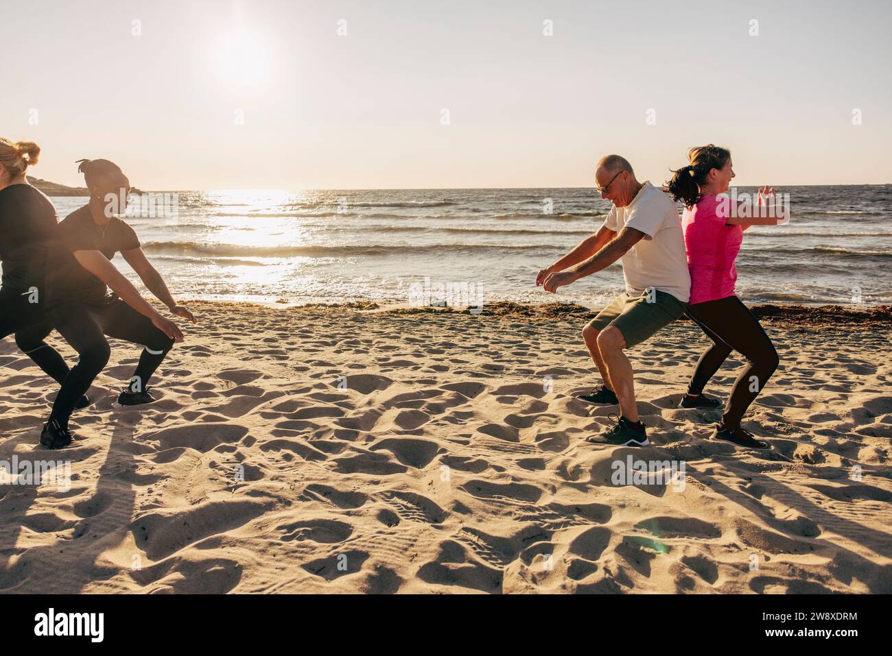 Team exercising with each other on sand during group training session ...
