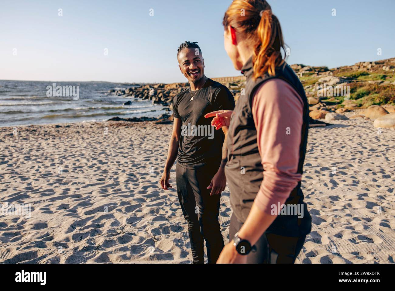 Side of woman talking with young man while standing on sand during ...