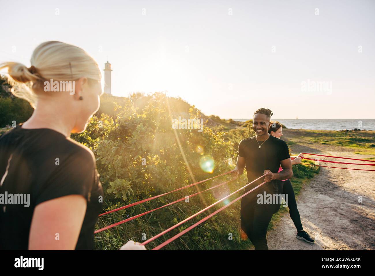 Smiling young man pulling resistance band while exercising with woman ...