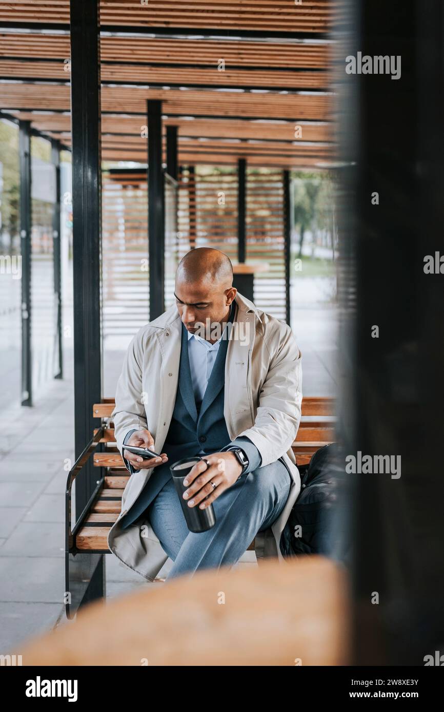 Male Business Professional Using Smart Phone While Sitting On Bench At