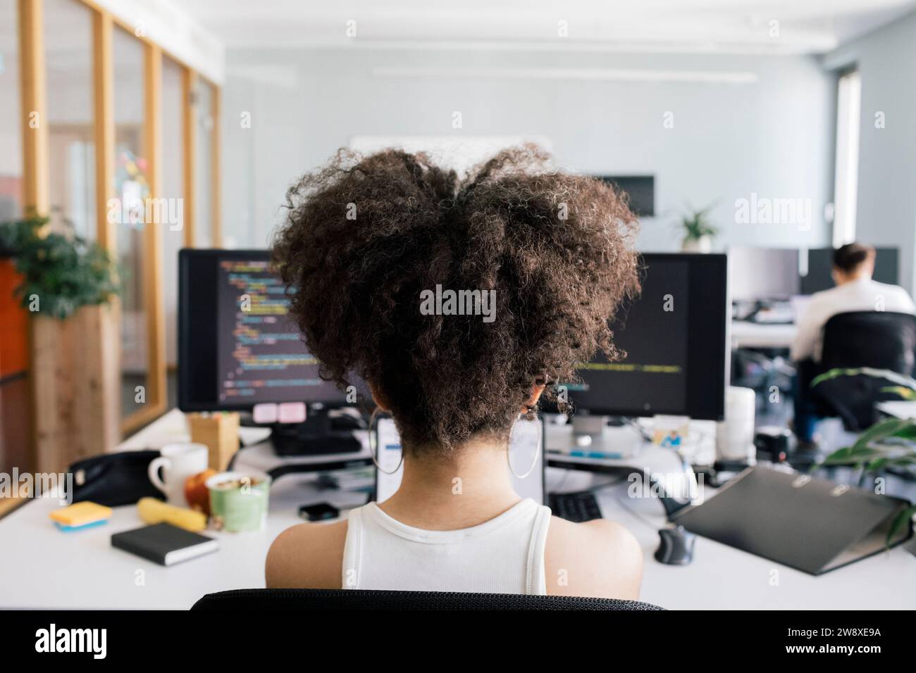 Female computer programmer with curly hair sitting at desk in office ...
