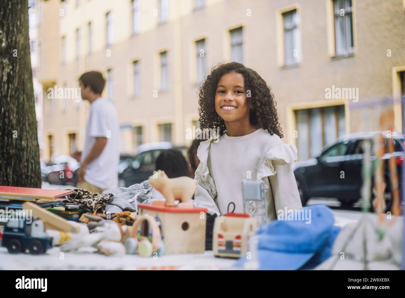 Portrait of smiling elementary girl standing near stall at flea market ...