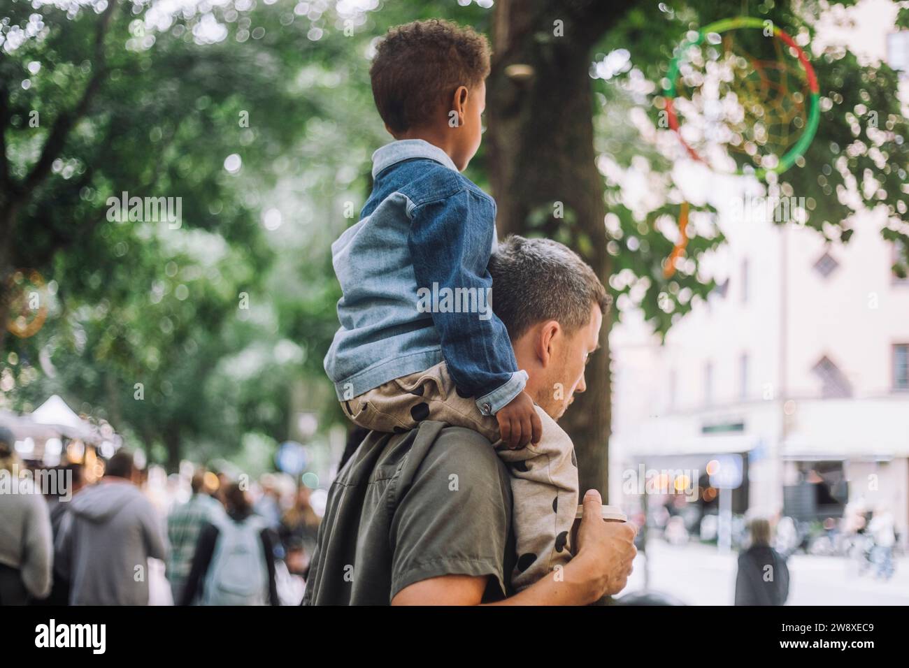 Side view of boy sitting on father's shoulder while shopping at flea ...