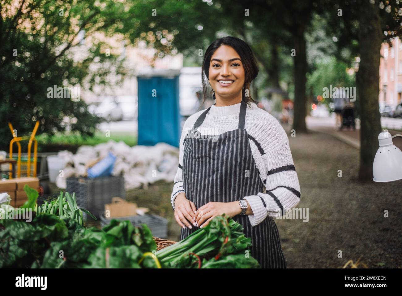 Portrait of smiling female vendor wearing apron while standing near ...