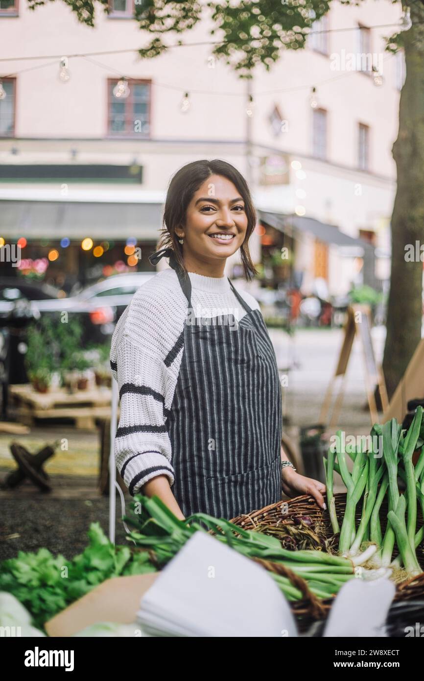 Portrait of smiling female vendor selling vegetables at organic market ...