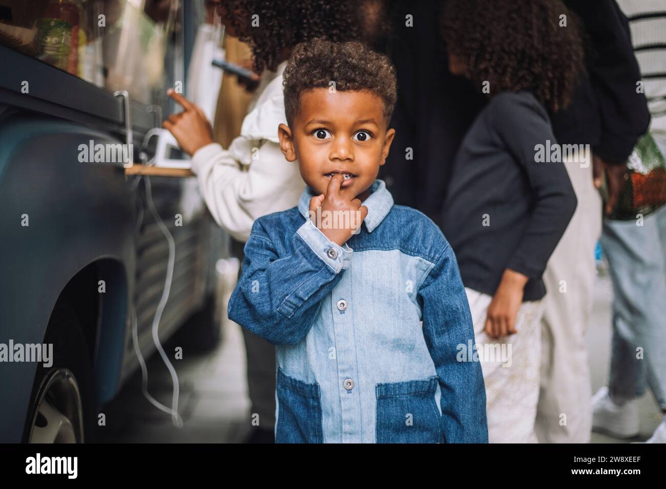 Portrait of mischievous boy standing with finger in mouth near food ...