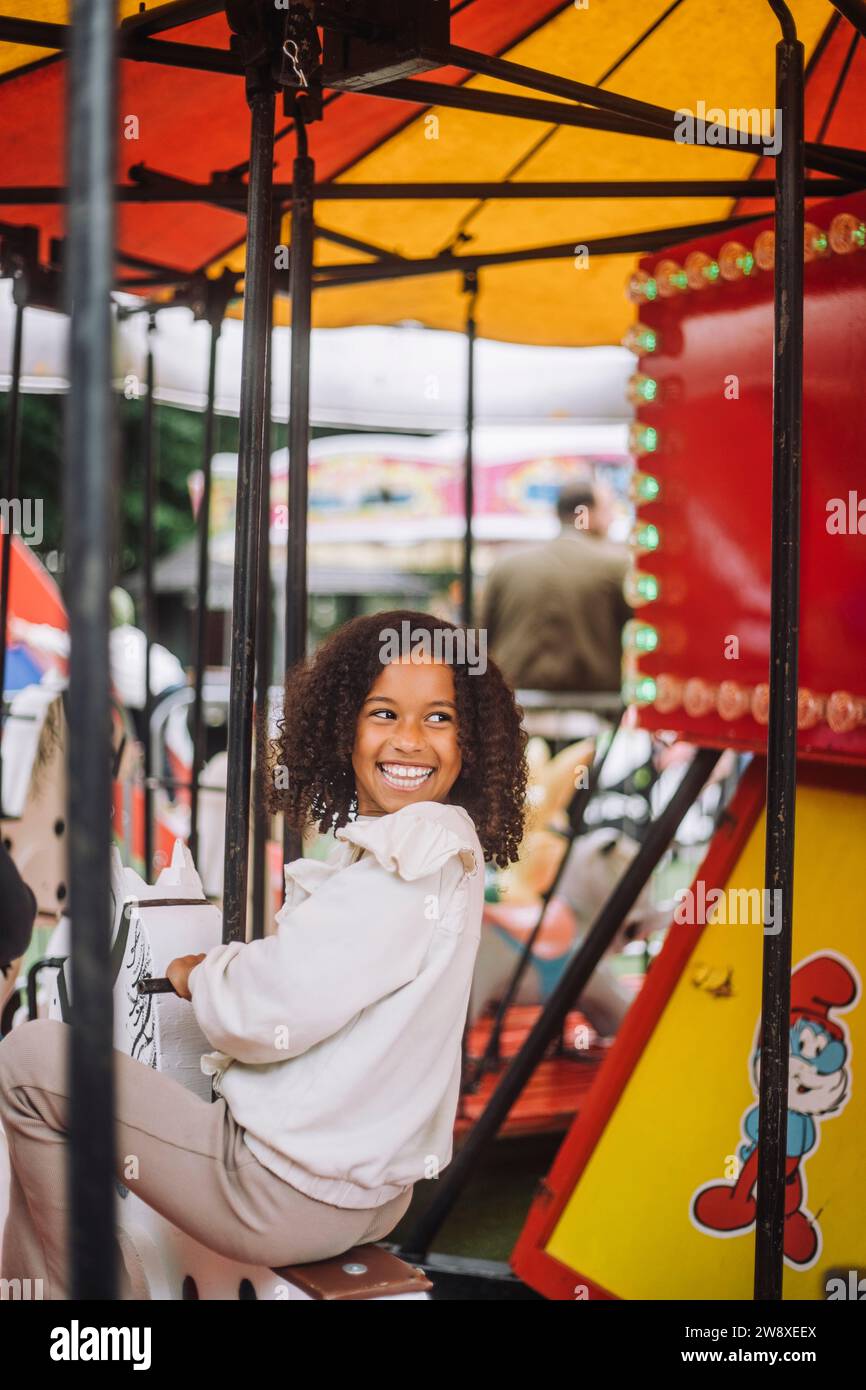 Happy girl looking over shoulder while having fun on carousel at ...