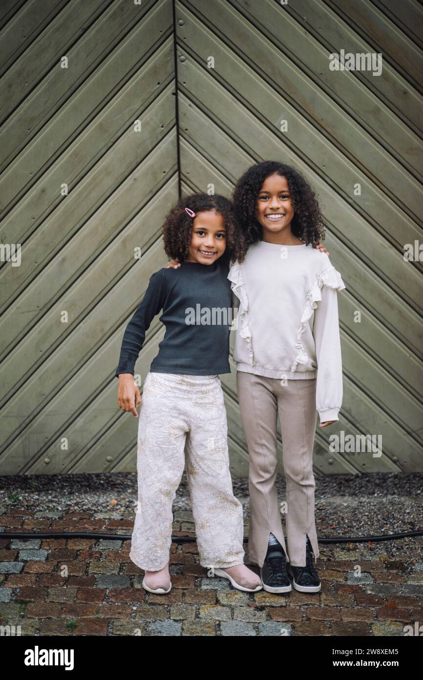 Portrait of smiling female siblings standing with arms around in front ...