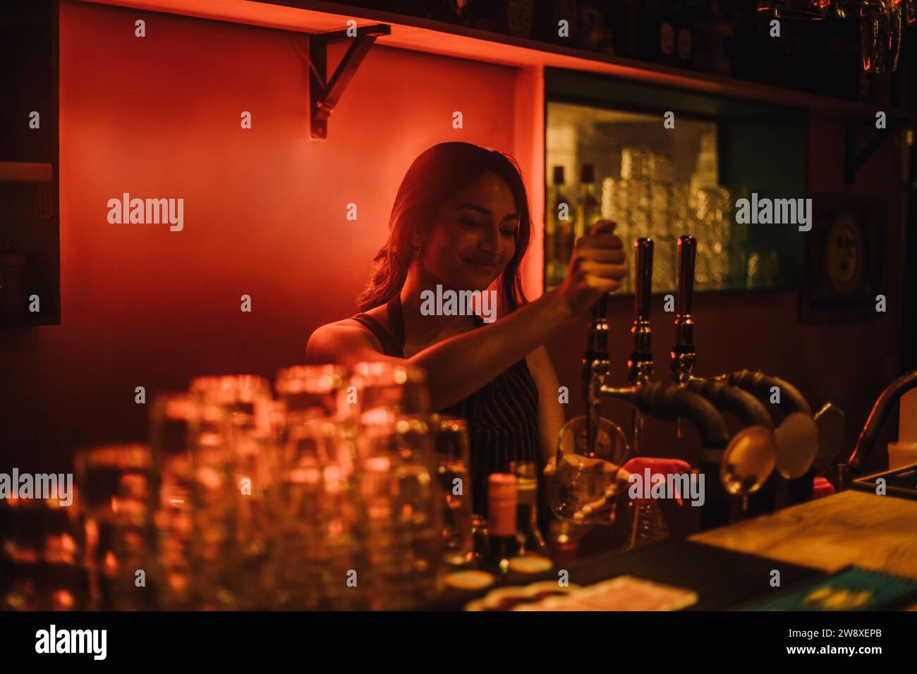 Female bartender filling beer in glass through tap while working at bar ...