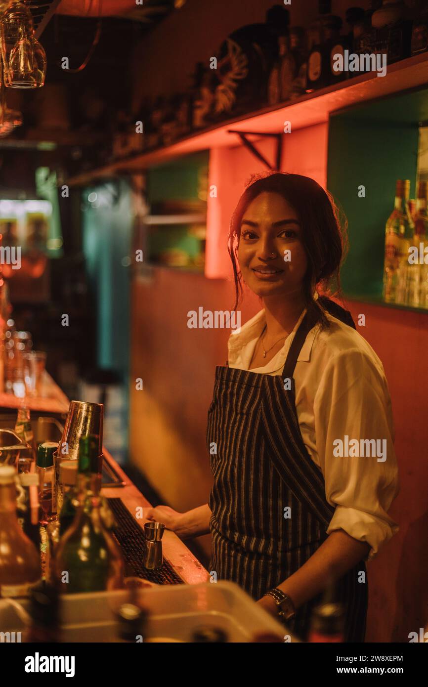 Portrait of smiling female bartender wearing apron and standing at bar ...