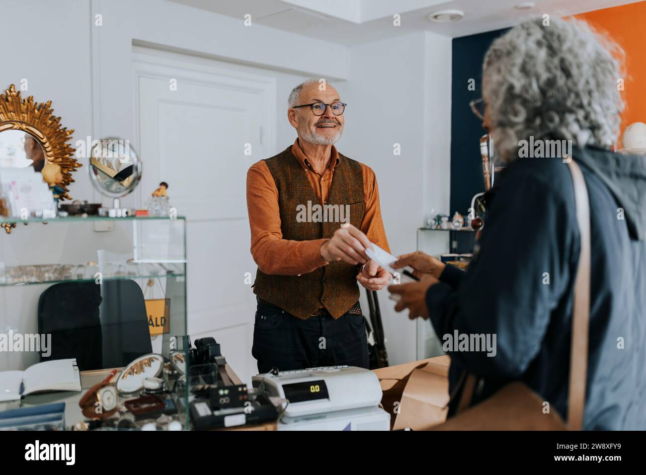 Male antique shop owner giving bill to female customer at counter in ...