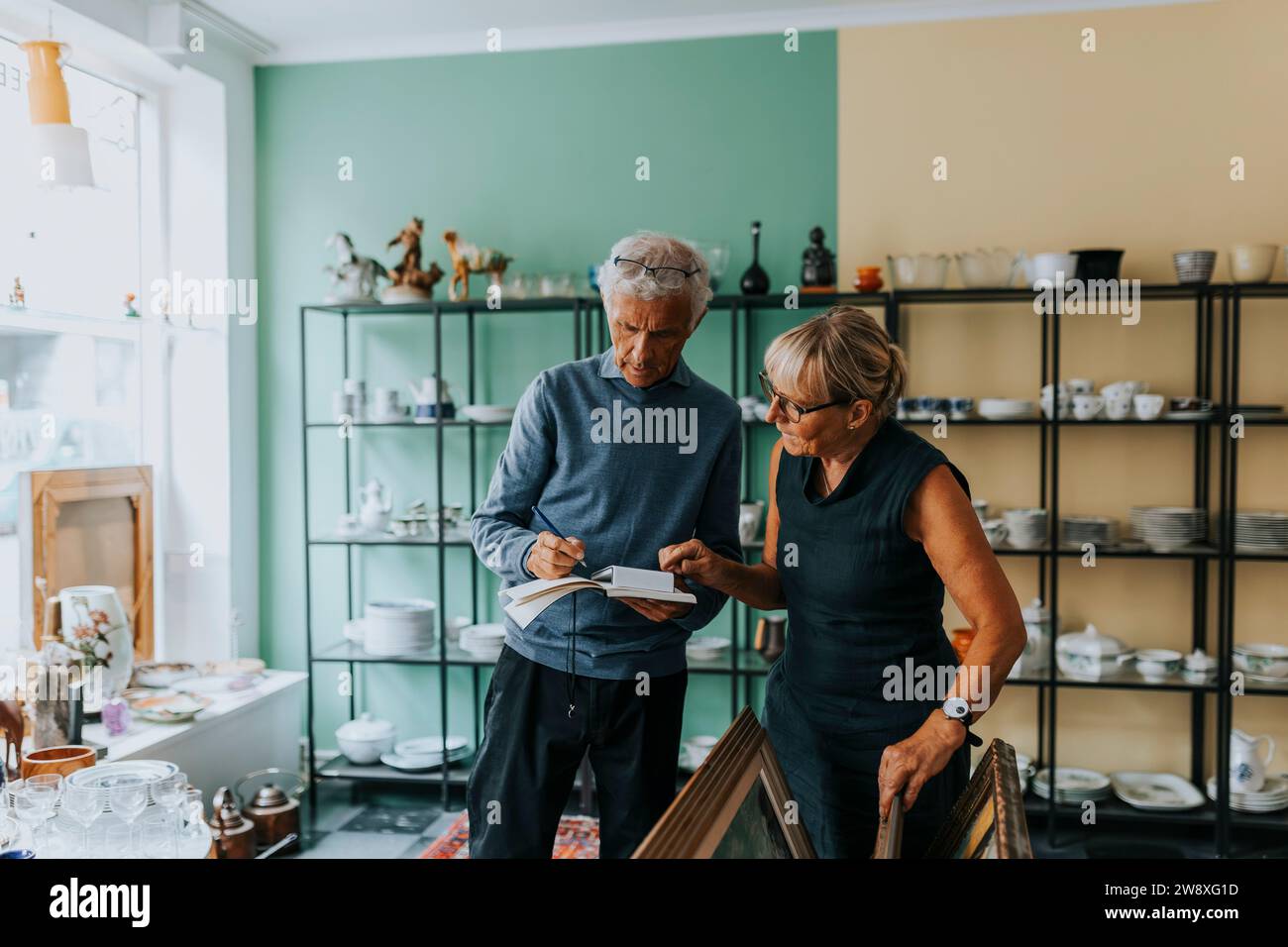 Female and male owners calculating while working in antique shop Stock ...