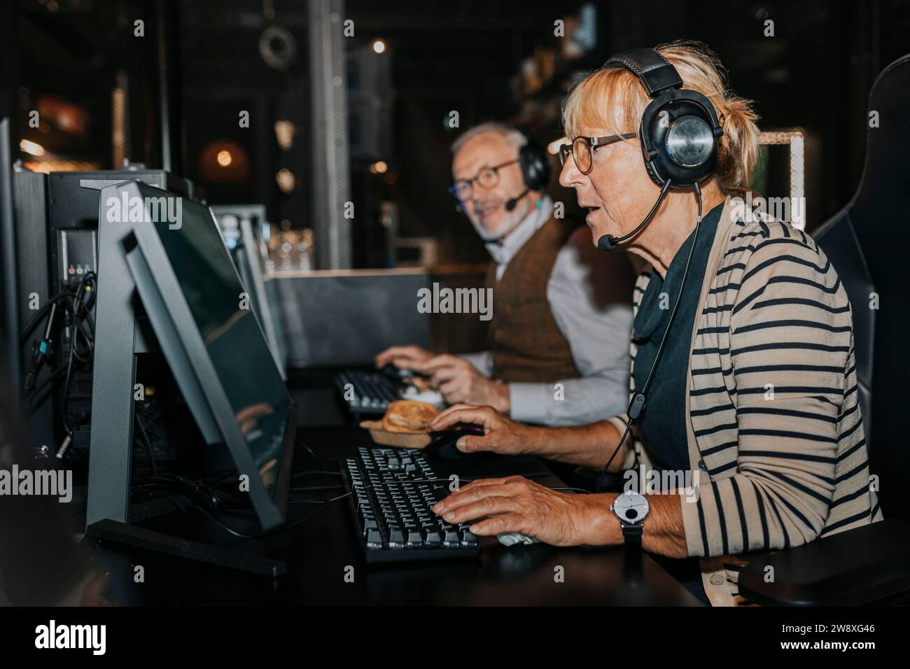 Senior woman playing video game on computer by male friend at gaming ...