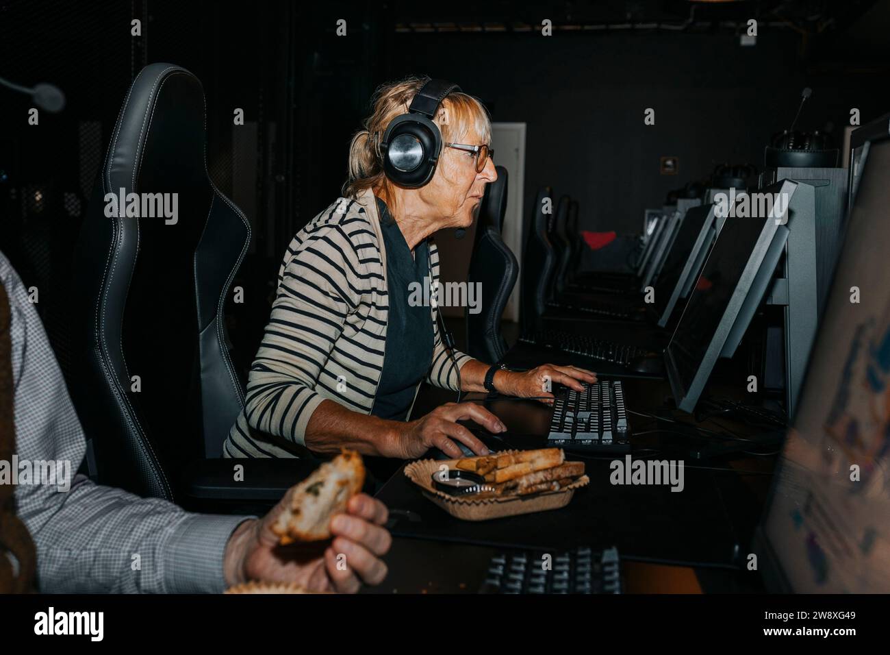 Elderly woman playing video game on computer by male friend at gaming ...