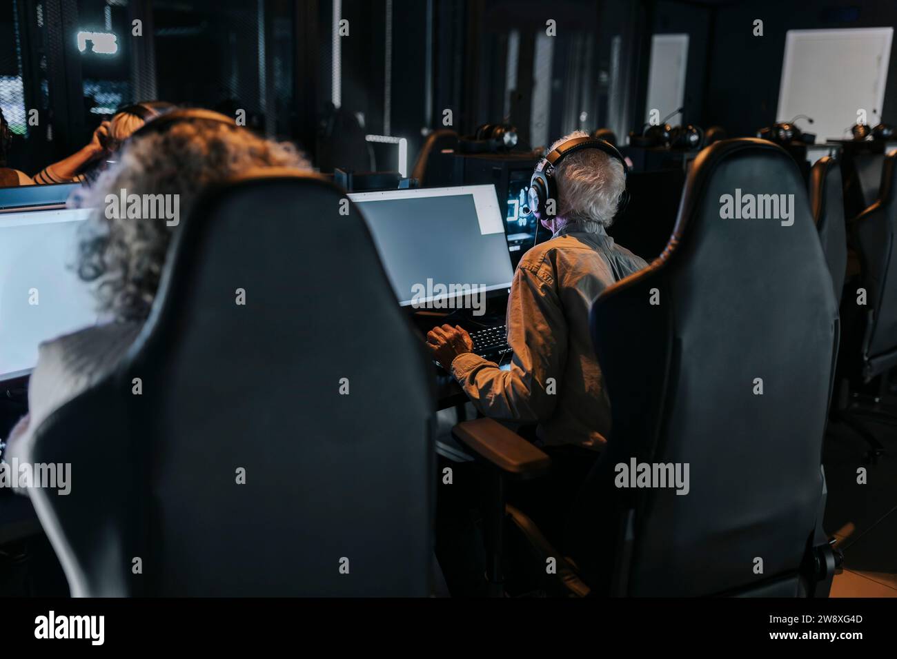 Rear view of male and female friends playing game over computers while ...