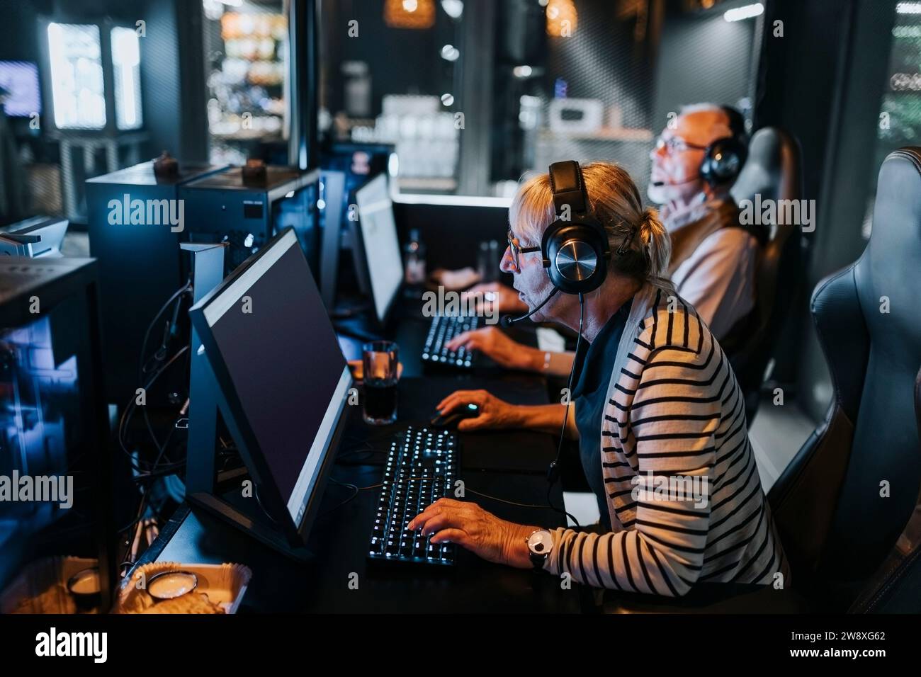 Elderly woman playing video game on computer by male friend at gaming ...
